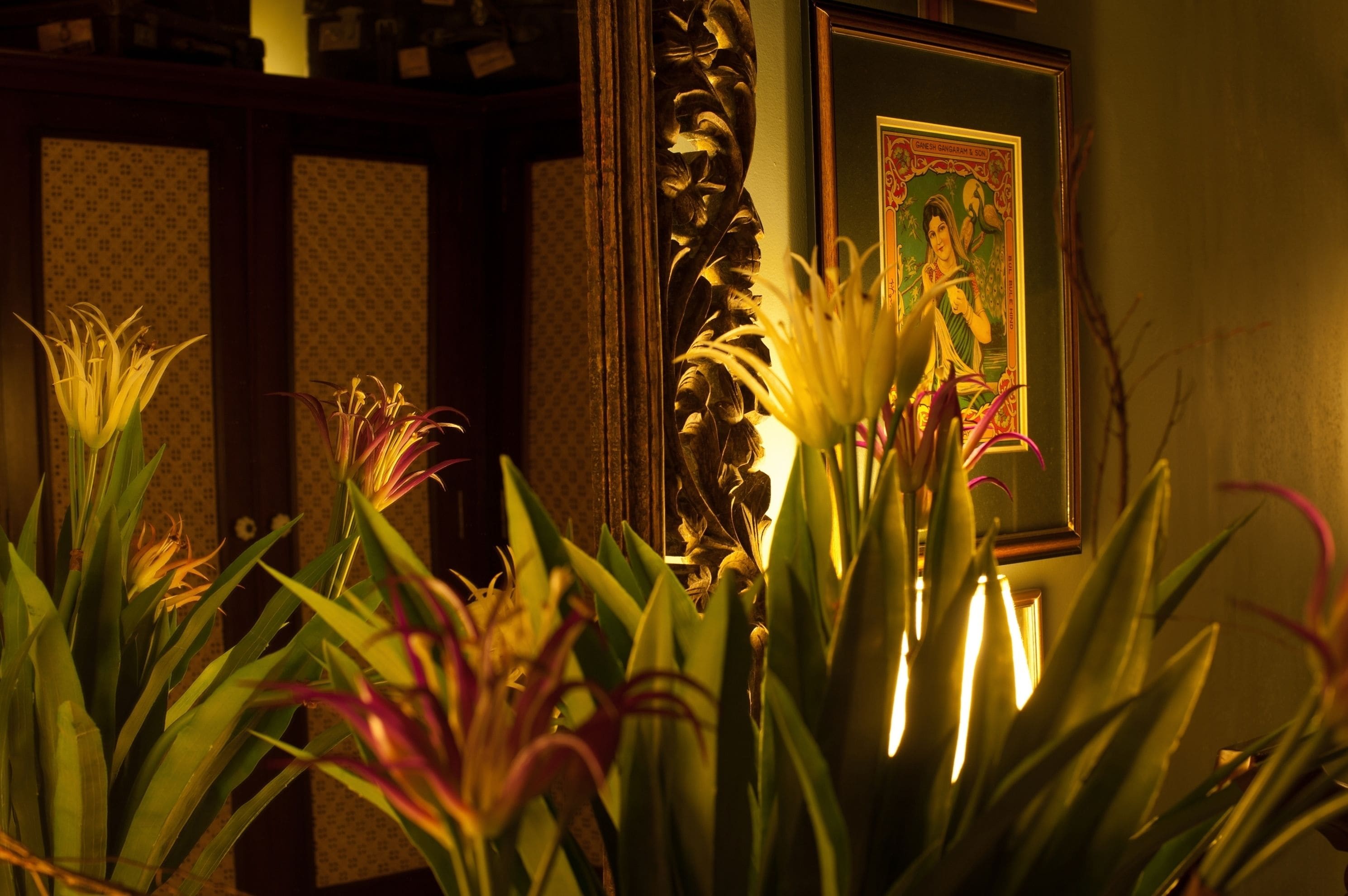 Um quarto com um quadro na parede, um armário de madeira e um vaso com flores amarelas e vermelhas.