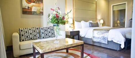 Quarto de hotel com cama, sofá, mesa de centro e um quadro na parede.
