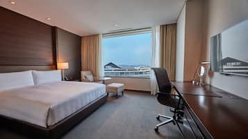 Quarto de hotel com uma cama grande, uma escrivaninha, uma cadeira, uma mesinha e uma televisão.