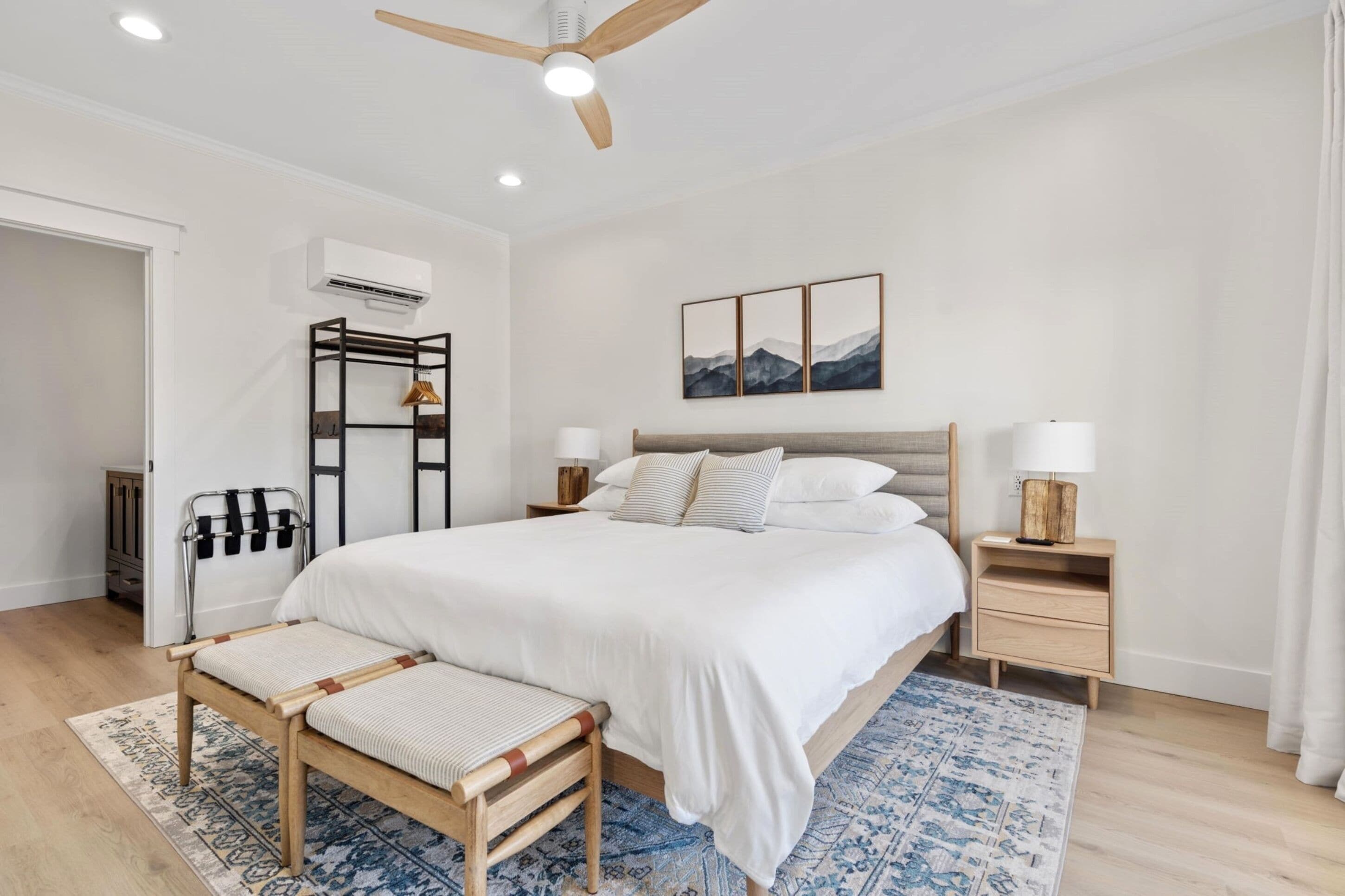Quarto moderno com uma cama grande, piso de madeira e um ventilador de teto.