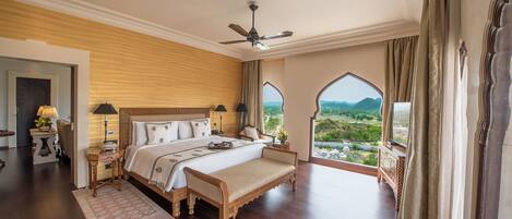 Um quarto espaçoso com uma cama grande, um ventilador de teto e vista para uma paisagem montanhosa através de janelas em arco.