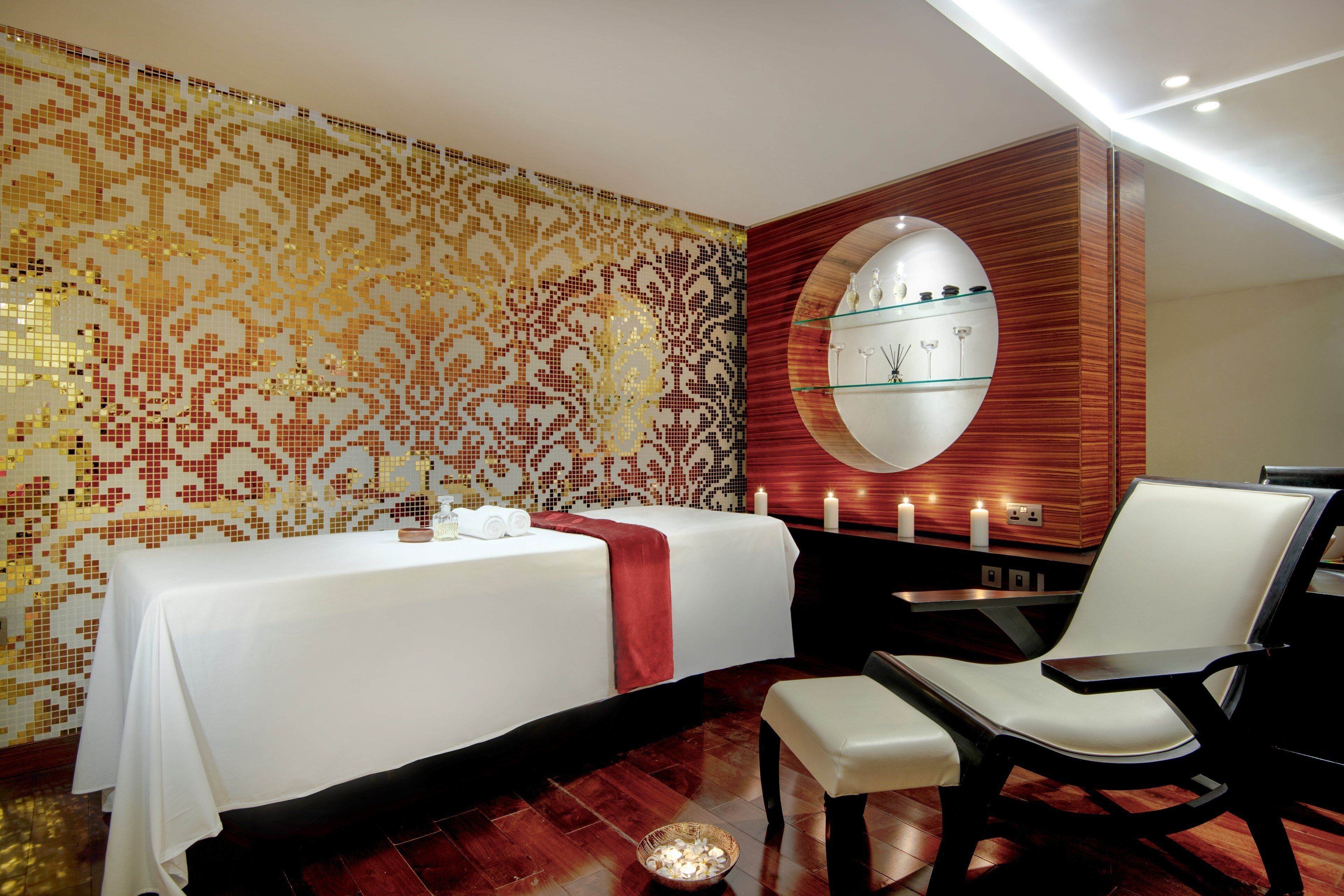 Quarto de hotel com cama branca, manta vermelha, aparador de madeira com velas e espelho redondo.