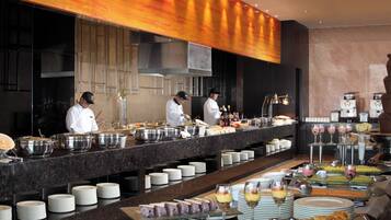 Buffet montado com diversas estações de serviço, uma variedade de pratos e uma cozinha moderna ao fundo.