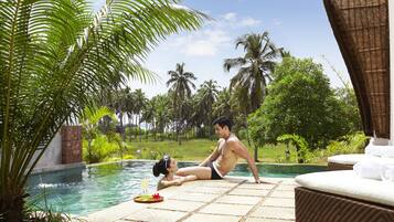 Uma área à beira da piscina com um homem e uma mulher relaxando, em meio à vegetação exuberante e palmeiras.