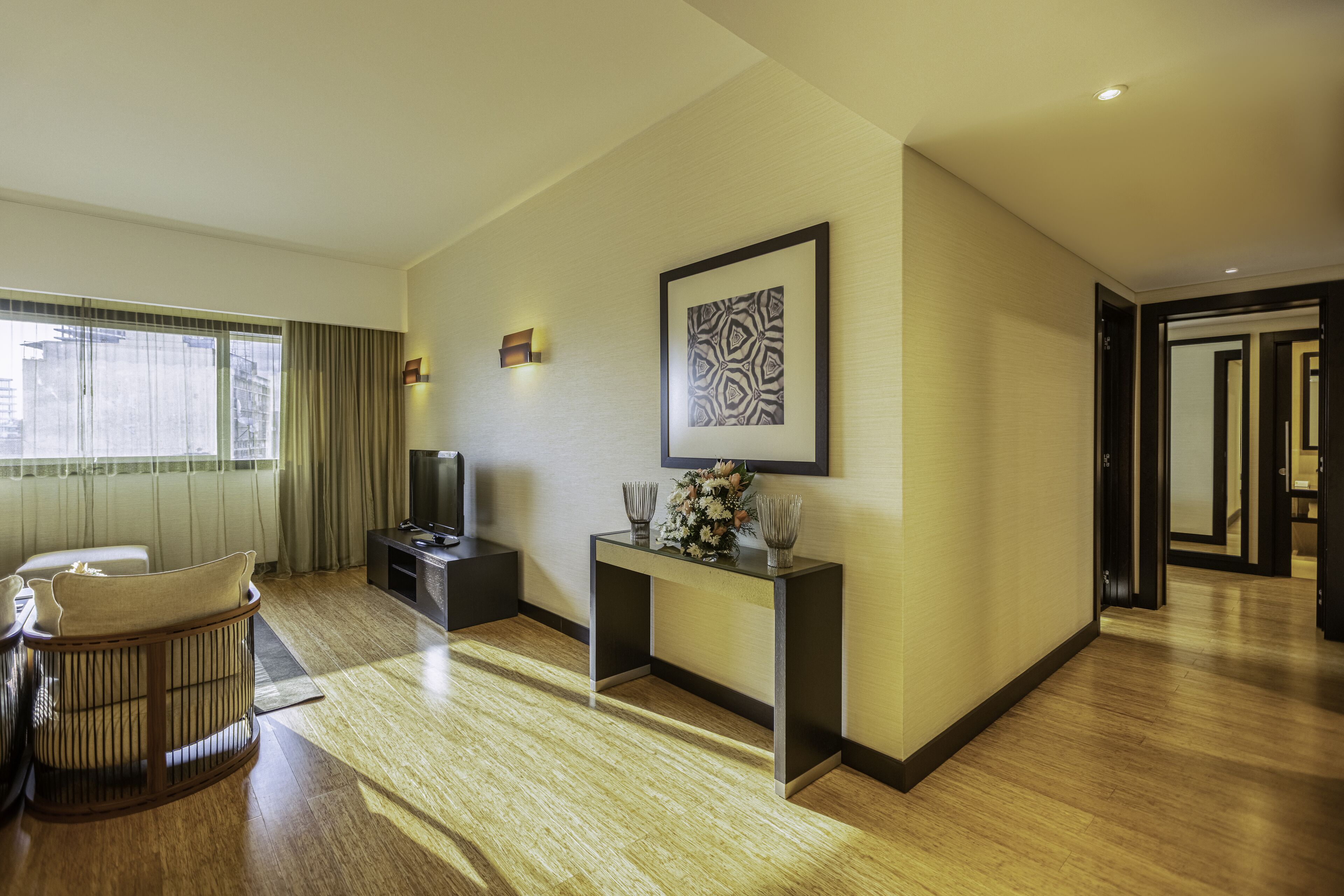 Uma sala de estar moderna com piso de madeira, um sofá, uma mesinha lateral com um vaso e um quadro na parede.
