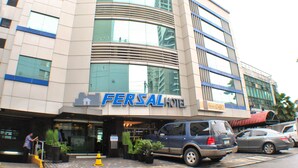 Um hotel com design moderno, exibindo uma placa grande com a inscrição 'FERSAL HOTEL', janelas amplas e uma área de estacionamento com vários carros.