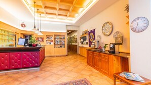 Um hall de hotel com um balcão de recepção vermelho, armários de madeira, uma máquina de café e um relógio na parede.