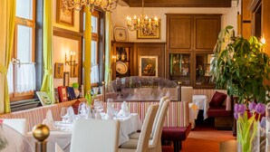 Um restaurante com assentos em cabines listradas, um candelabro e um espelho grande.