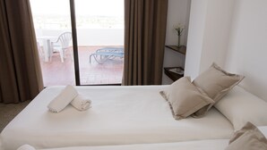 Quarto de hotel com uma cama grande, vista para o terraço e uma pequena mesa com cadeiras.
