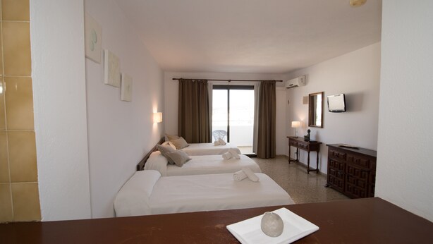 Quarto de hotel com duas camas, uma escrivaninha, cômoda, televisão e janela com cortinas.