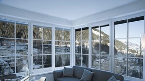 Quarto aconchegante com um sofá cinza e uma janela grande com vista para uma montanha nevada.