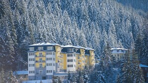 Um hotel de vários andares com fachada amarela e branca, rodeado por árvores cobertas de neve.