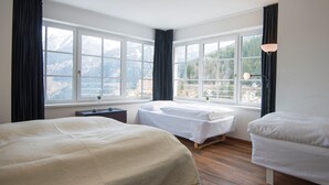 Quarto de hotel com duas camas, mesa de cabeceira e janela com vista para as montanhas.