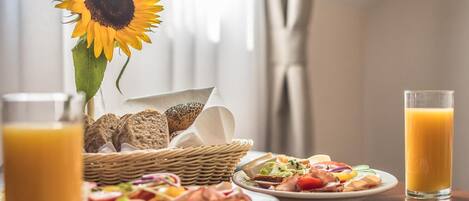 Um cenário de café da manhã com uma decoração em formato de sol, cesta de pão, pratos com comida e um copo de suco de laranja.
