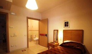 Quarto de hotel com cama, mesa de cabeceira e porta para um banheiro.