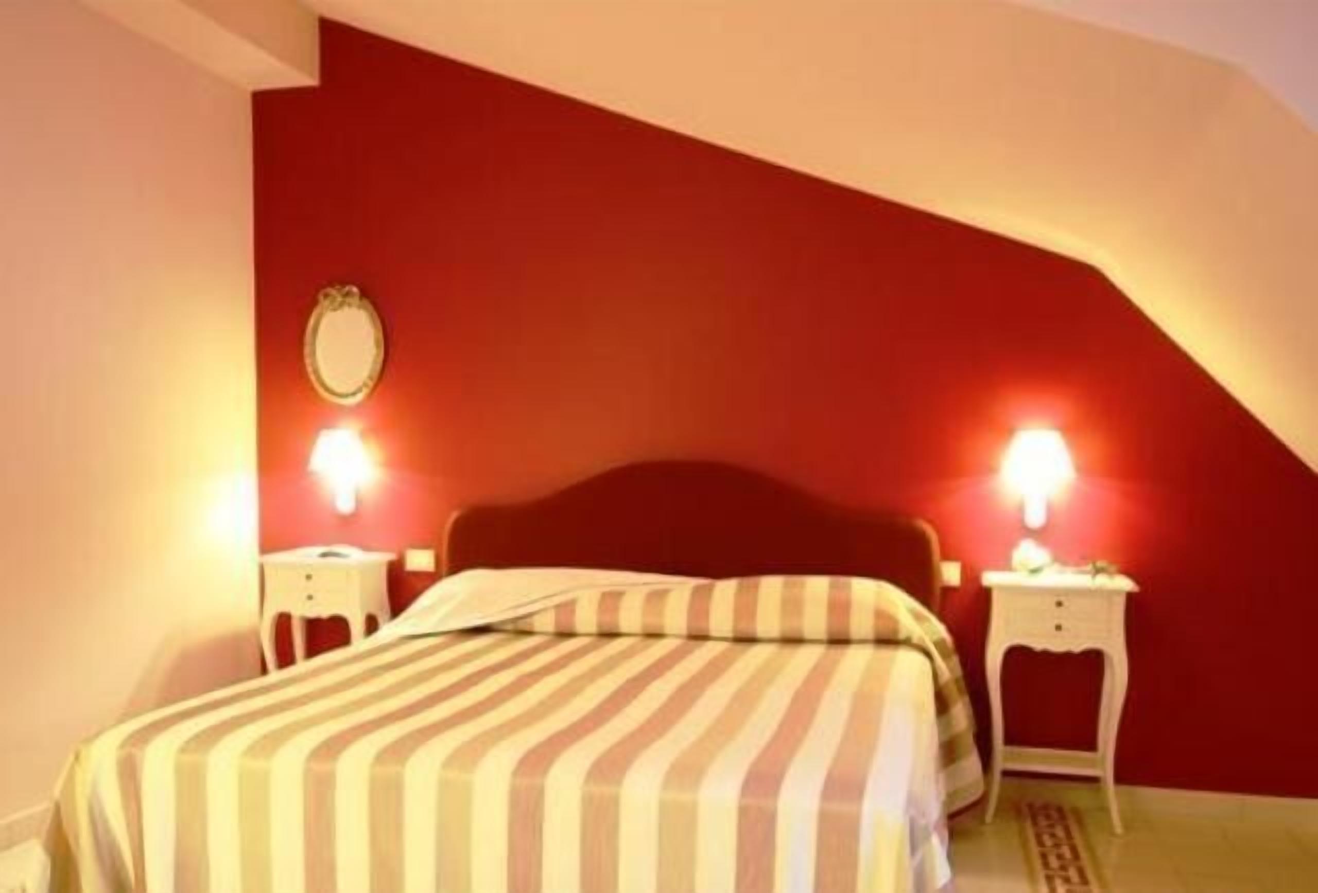 Quarto com parede vermelha, colcha listrada e duas luminárias de cabeceira.