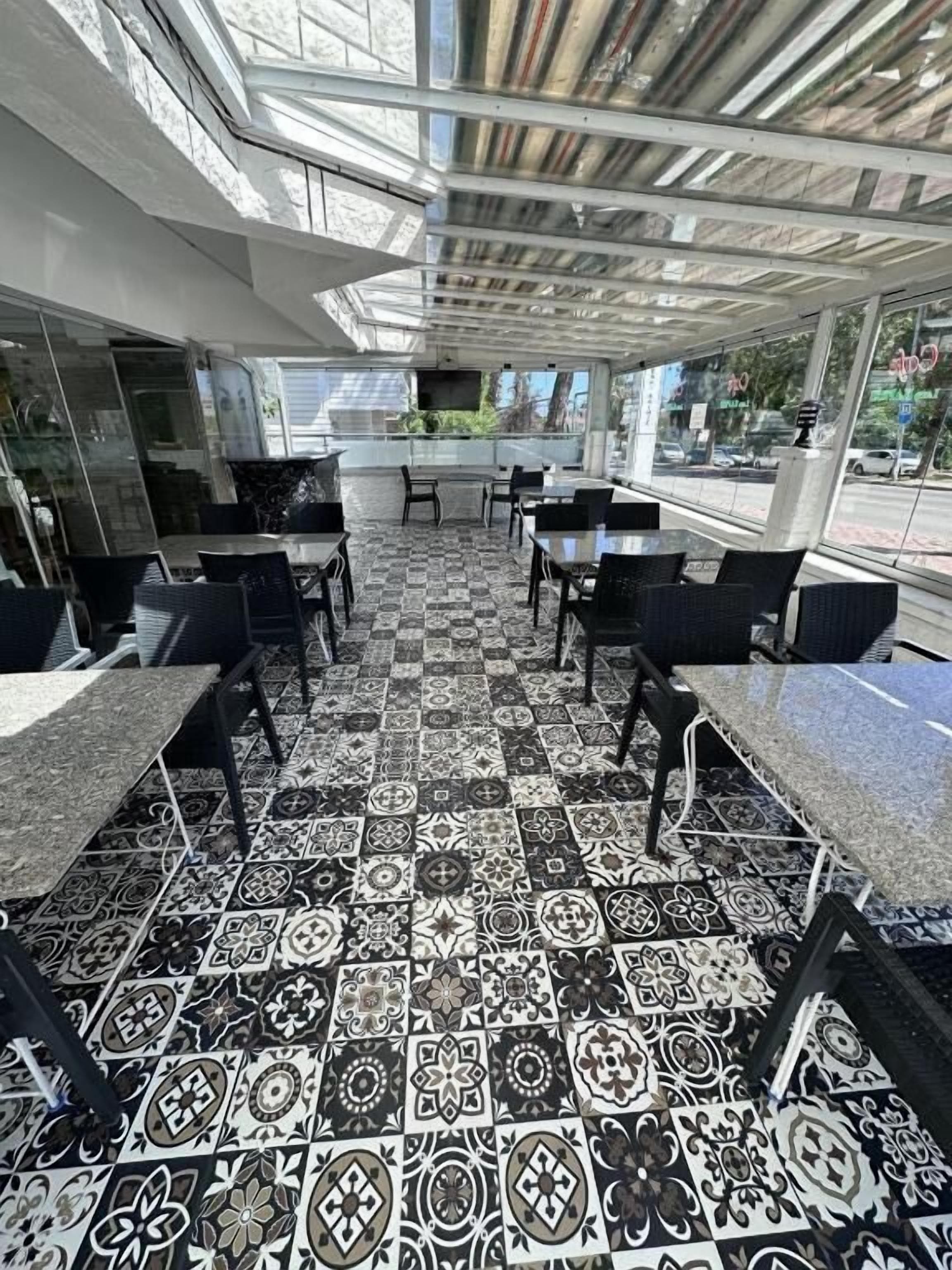 Um café ao ar livre com piso estampado, mesas e cadeiras.