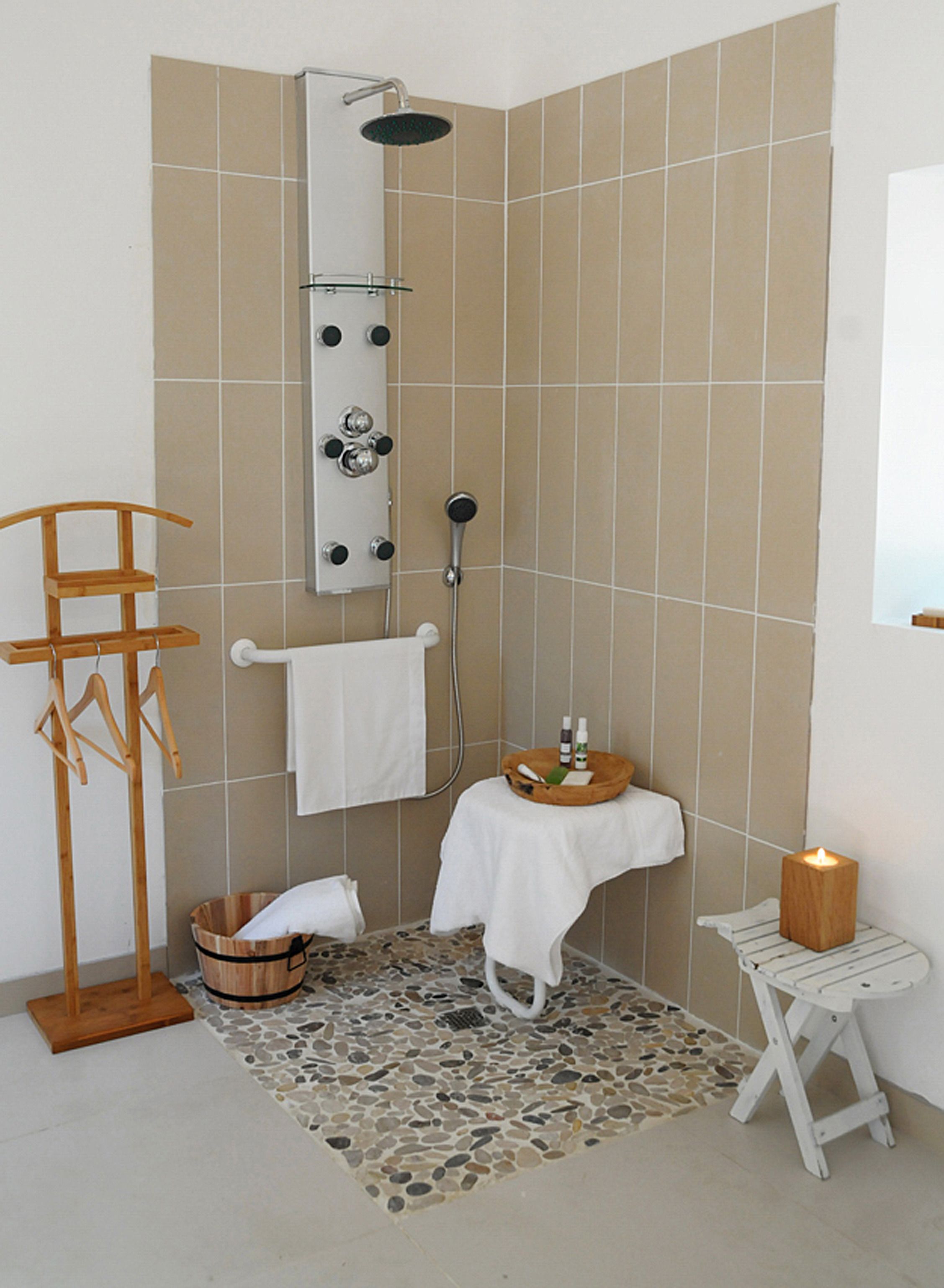 Casa de banho com chuveiro, um porta-toalhas, uma pequena mesa com artigos de higiene pessoal e um varal de madeira.