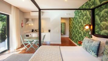 Quarto de hotel moderno com cama grande, cozinha compacta, espaço para refeições e vista para área verde.