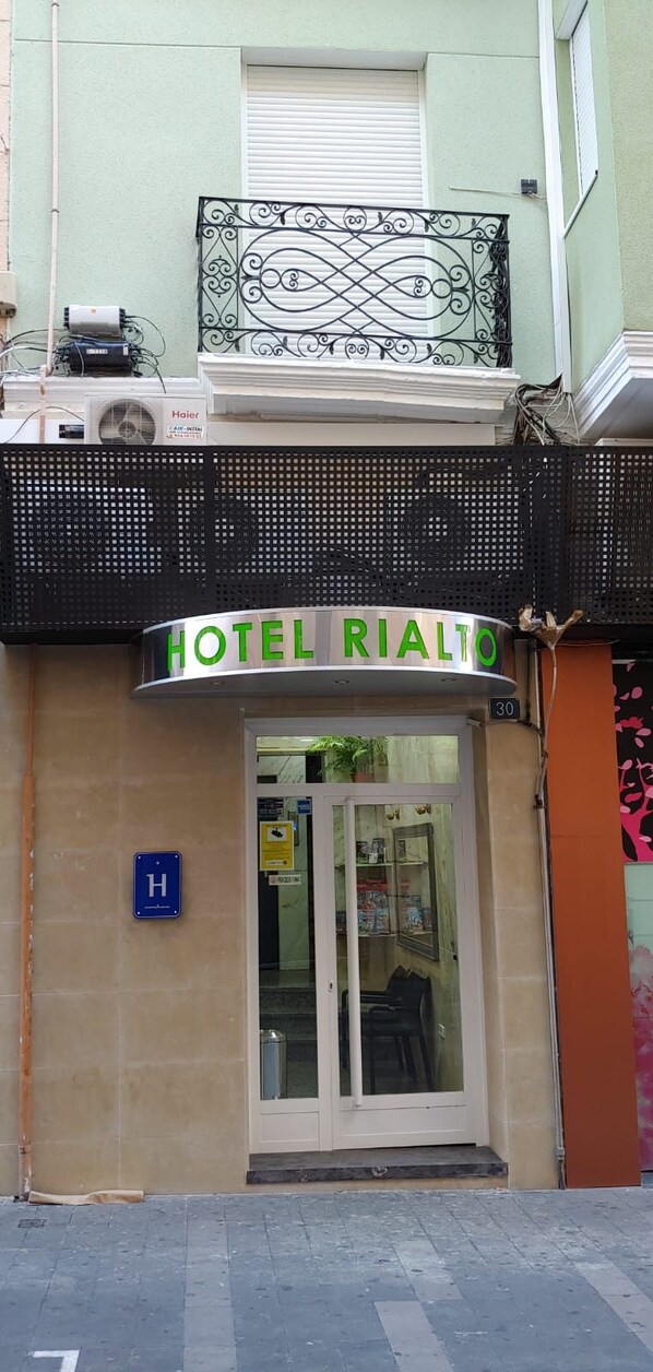 Entrada de hotel com uma placa indicando "HOTEL RIALTO" e um sinal azul de acessibilidade para pessoas com deficiência.