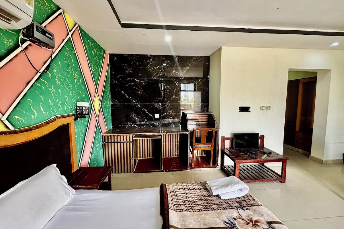 Quarto de hotel com cama, secretária, cadeira e televisão.