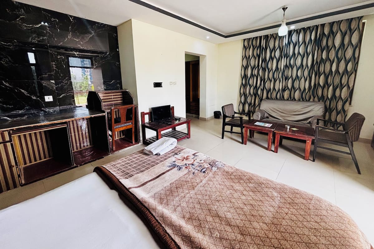 Quarto de hotel moderno com uma cama grande, área de estar com sofá e poltronas, televisão e uma parede de destaque em mármore.