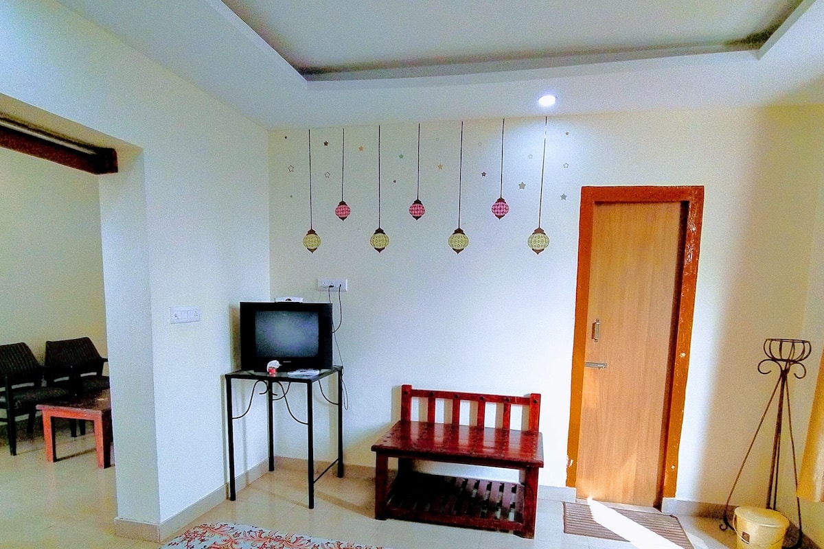 Uma sala de estar com televisão, um banco e uma porta.