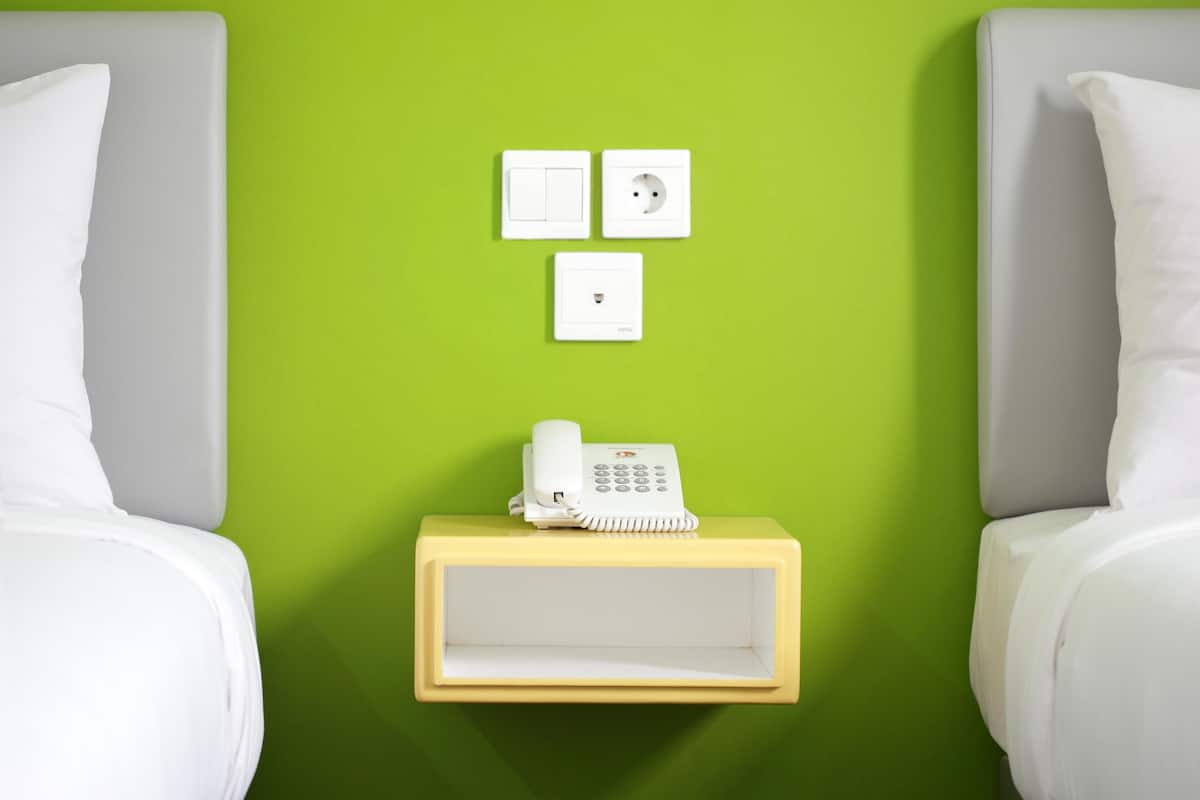 Quarto de hotel com duas camas, uma parede verde e um telefone ao lado da cama.