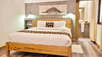 Uma cama de madeira com roupa de cama branca, um travesseiro estampado, um quadro na parede e um abajur.
