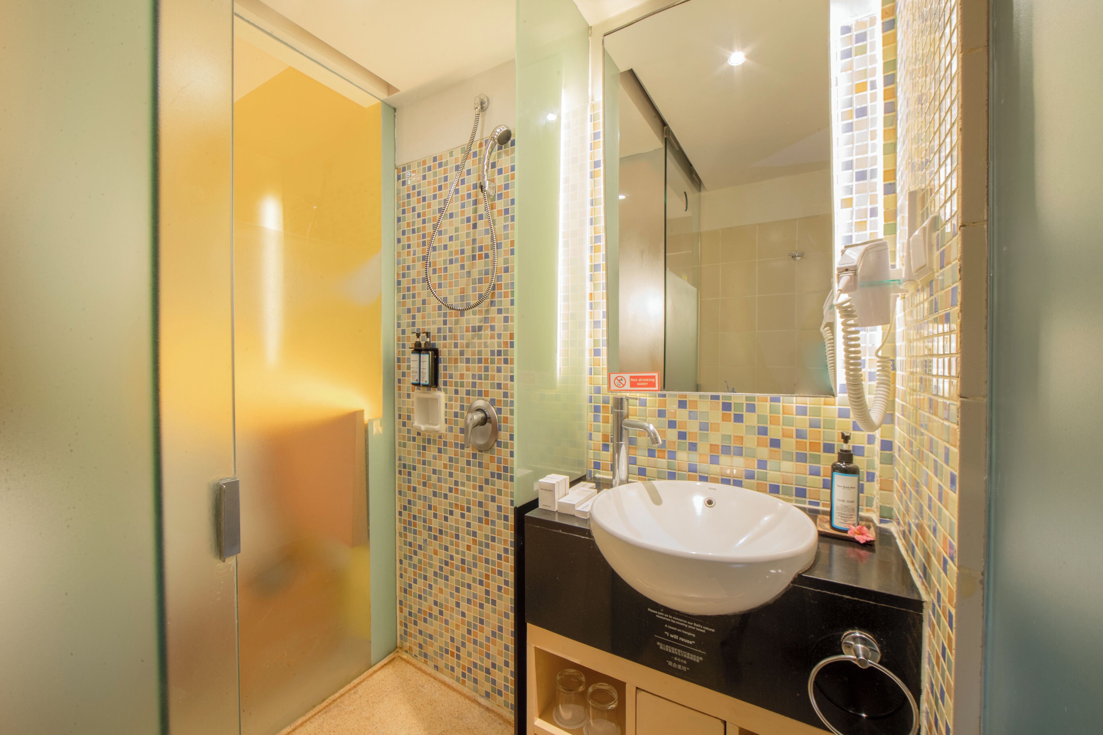 Casa de banho com cabine de duche em vidro, lavatório com bancada preta e espelho com painel de azulejos.