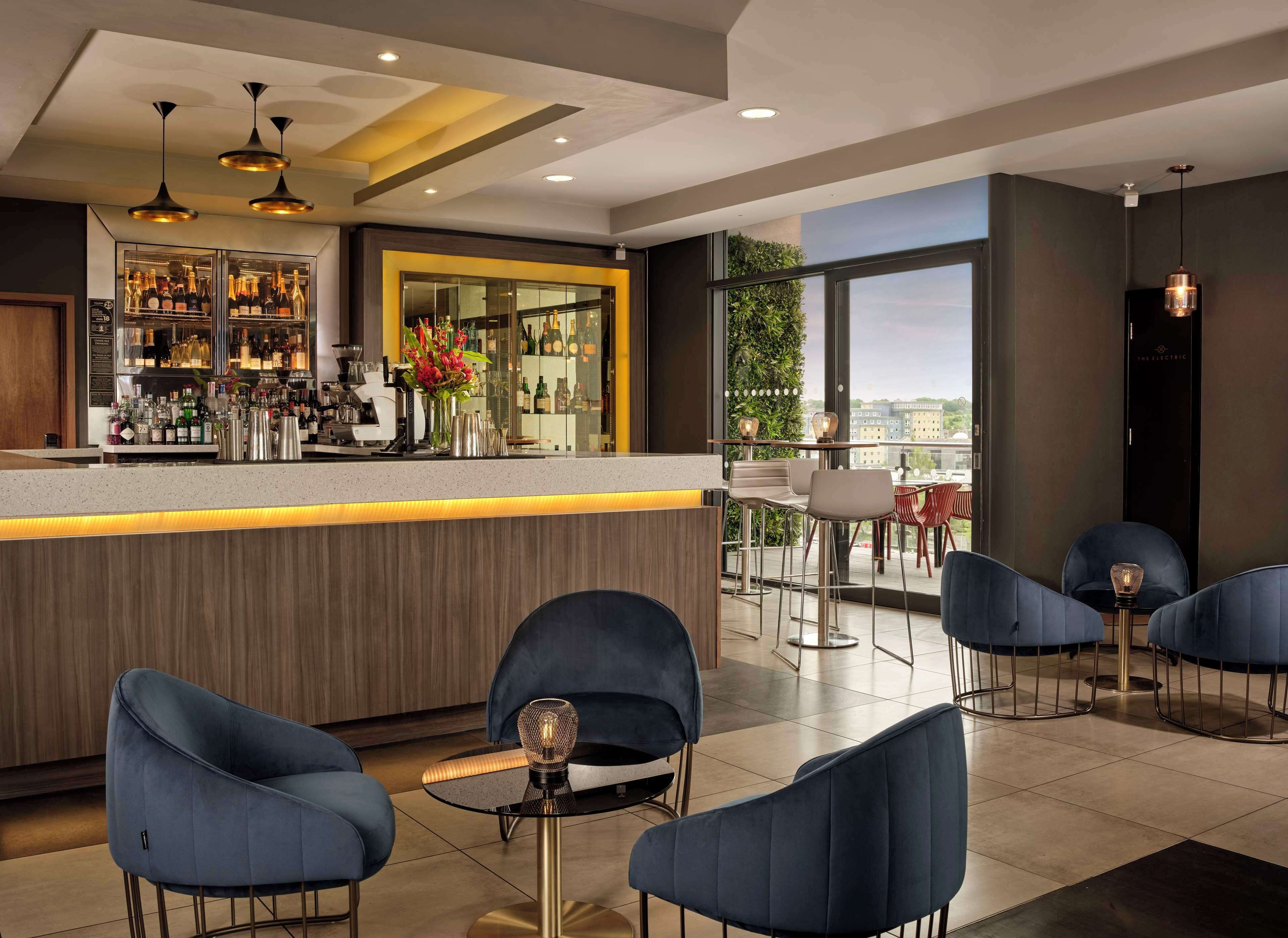 Uma área de bar moderna com balcão, banquetas e vista da cidade através de grandes janelas.