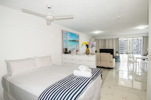 Quarto de hotel com cama, escrivaninha, cadeira, televisão e vista da cidade.