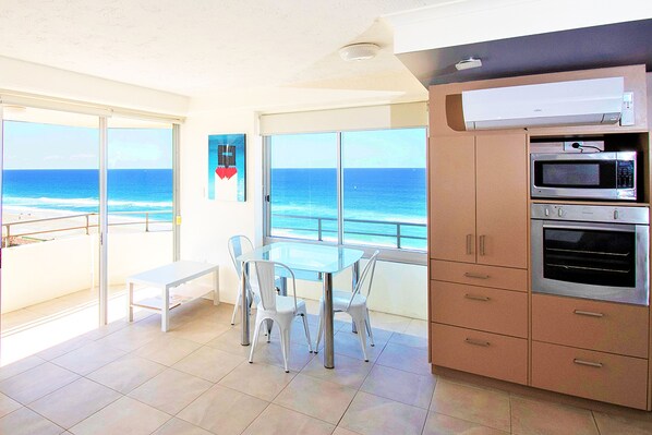 Varanda com vista para o oceano, área de refeições com mesa e cadeiras, e cozinha equipada.