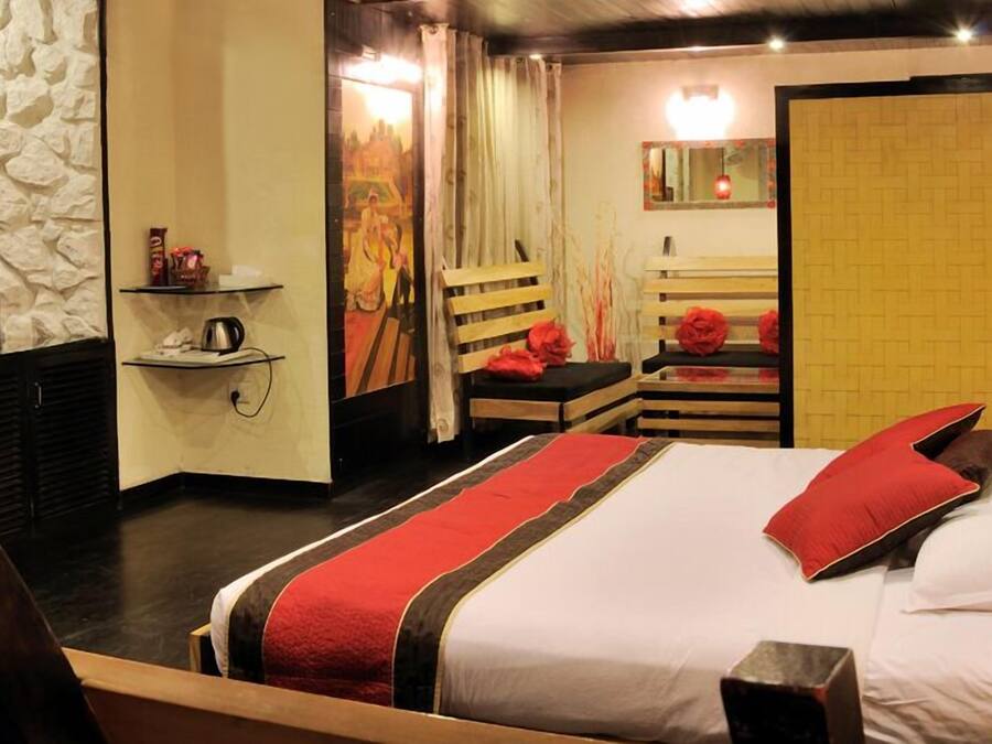 Quarto de hotel com cama, cabeceira de madeira, mesa de cabeceira, luminária e televisão fixada na parede.