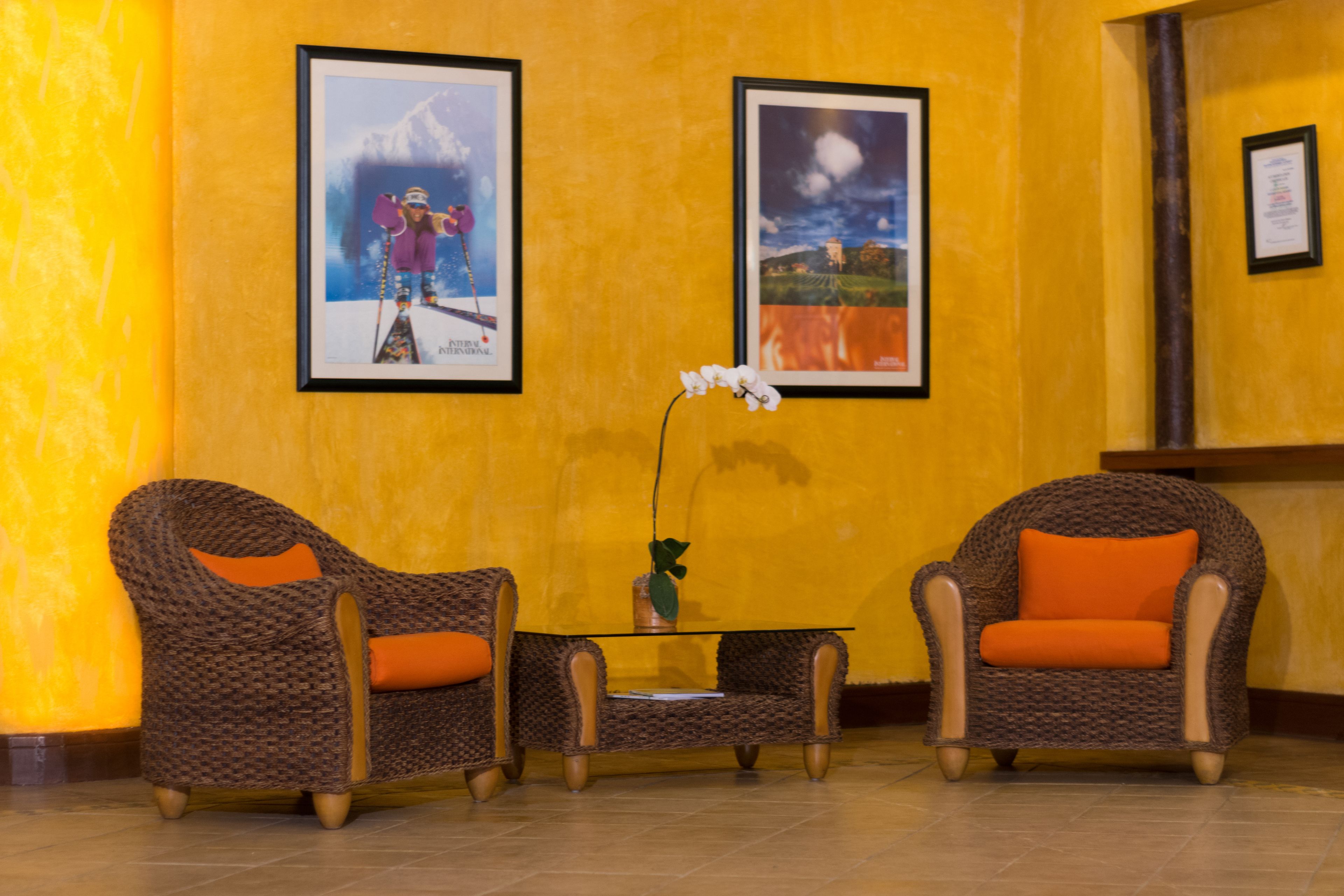 Um hall de entrada com cadeiras de vime, uma mesa de vidro e duas fotos emolduradas na parede.