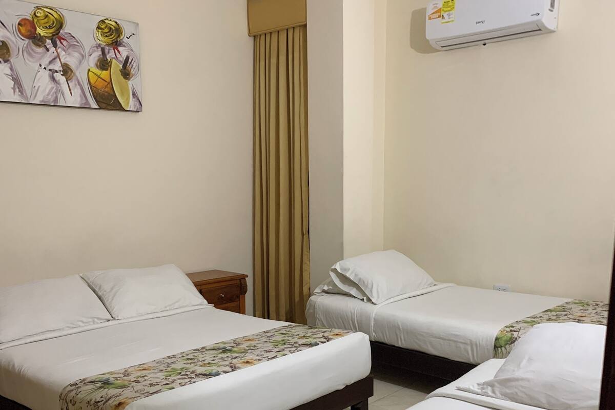 Quarto de hotel com duas camas, um quadro na parede, uma janela com cortinas e um aparelho de ar condicionado.