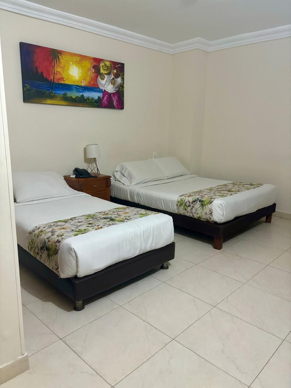 Quarto de hotel com duas camas, mesa de cabeceira, abajur e um quadro na parede.