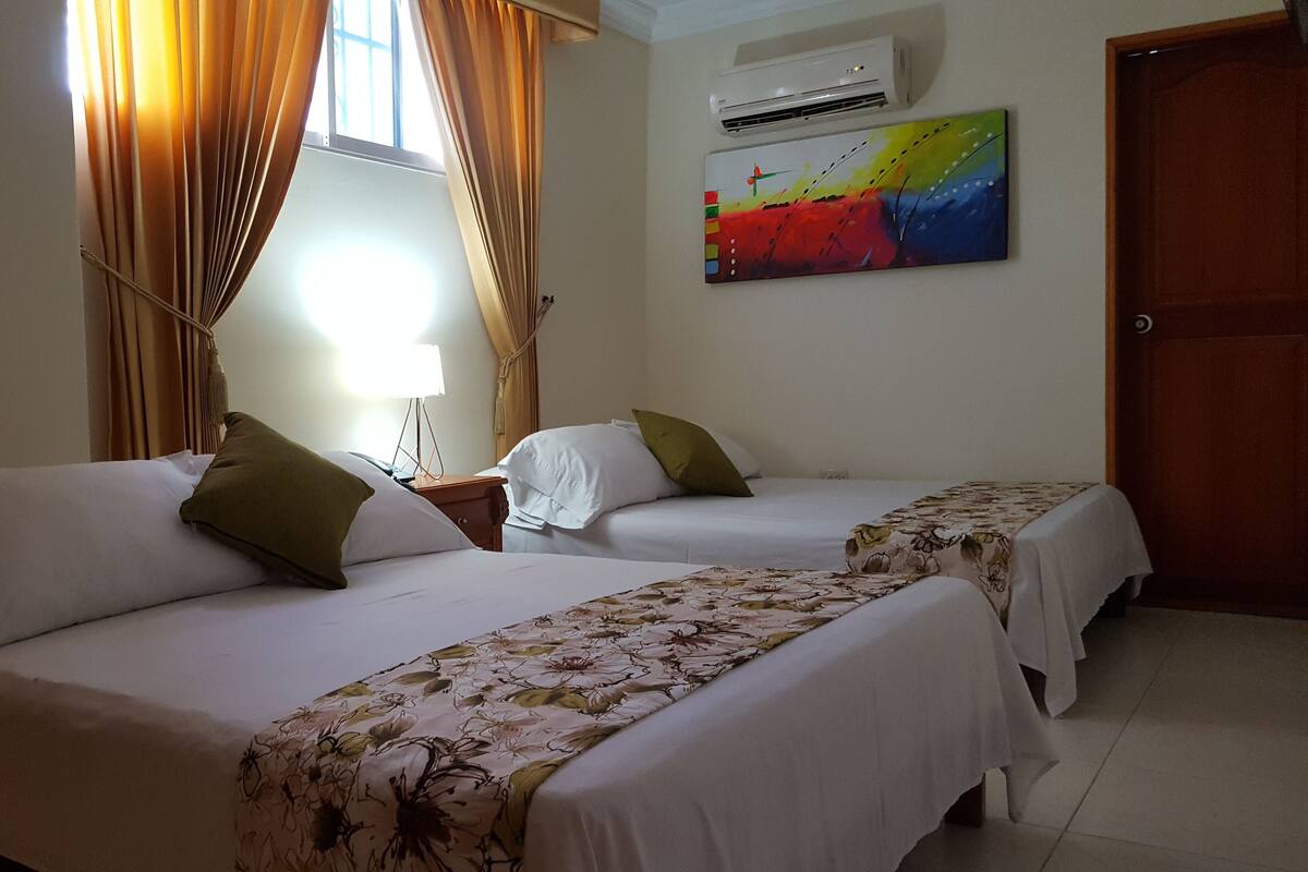 Quarto de hotel com duas camas, um quadro na parede e um aparelho de ar condicionado.