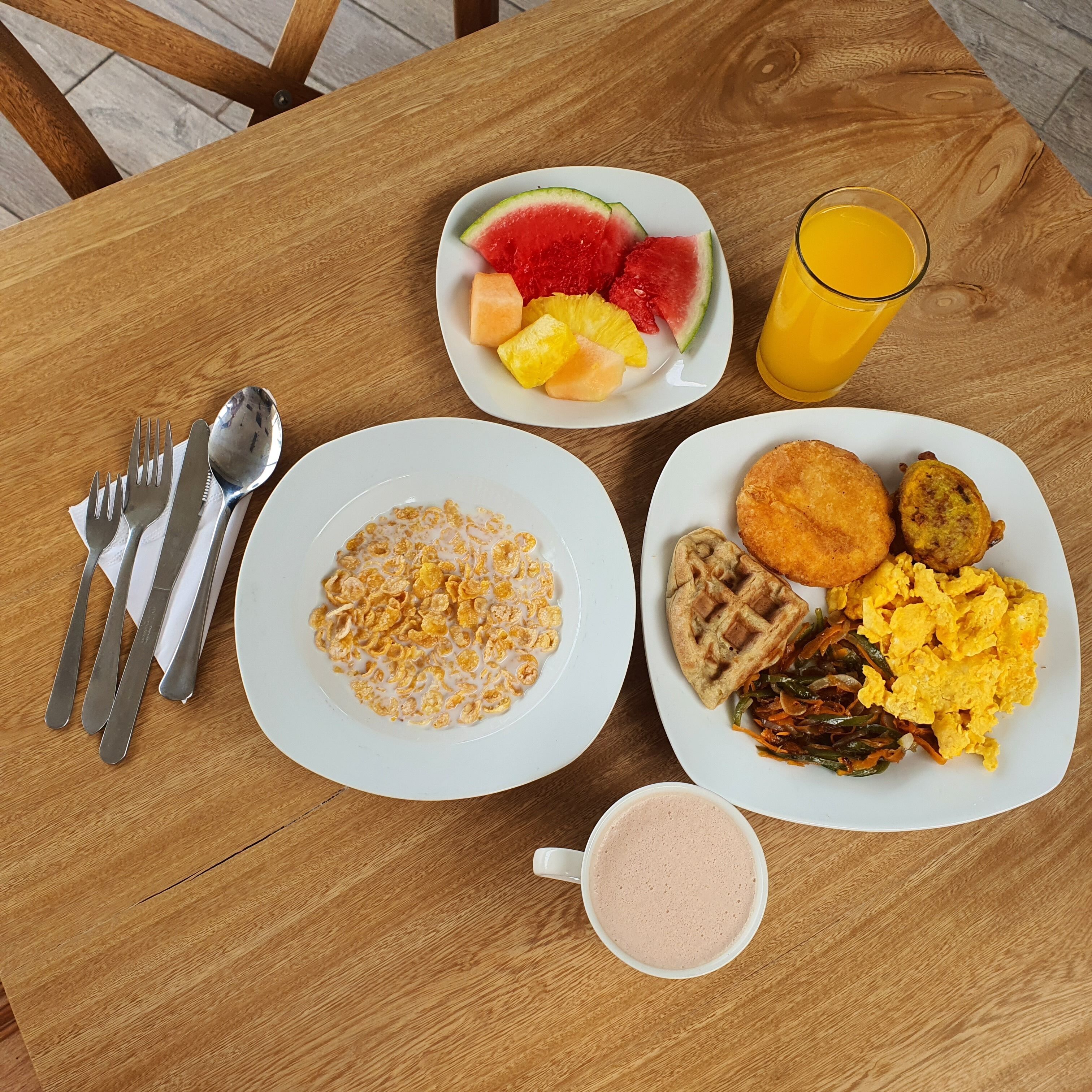 Uma mesa de café da manhã com cereal, waffles, ovos mexidos e um copo de suco de laranja.