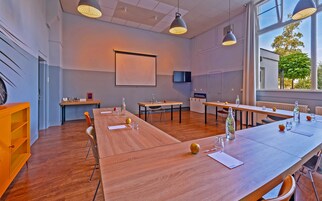 Uma sala de conferências com mesas de madeira, cadeiras, tela de projeção e uma televisão.