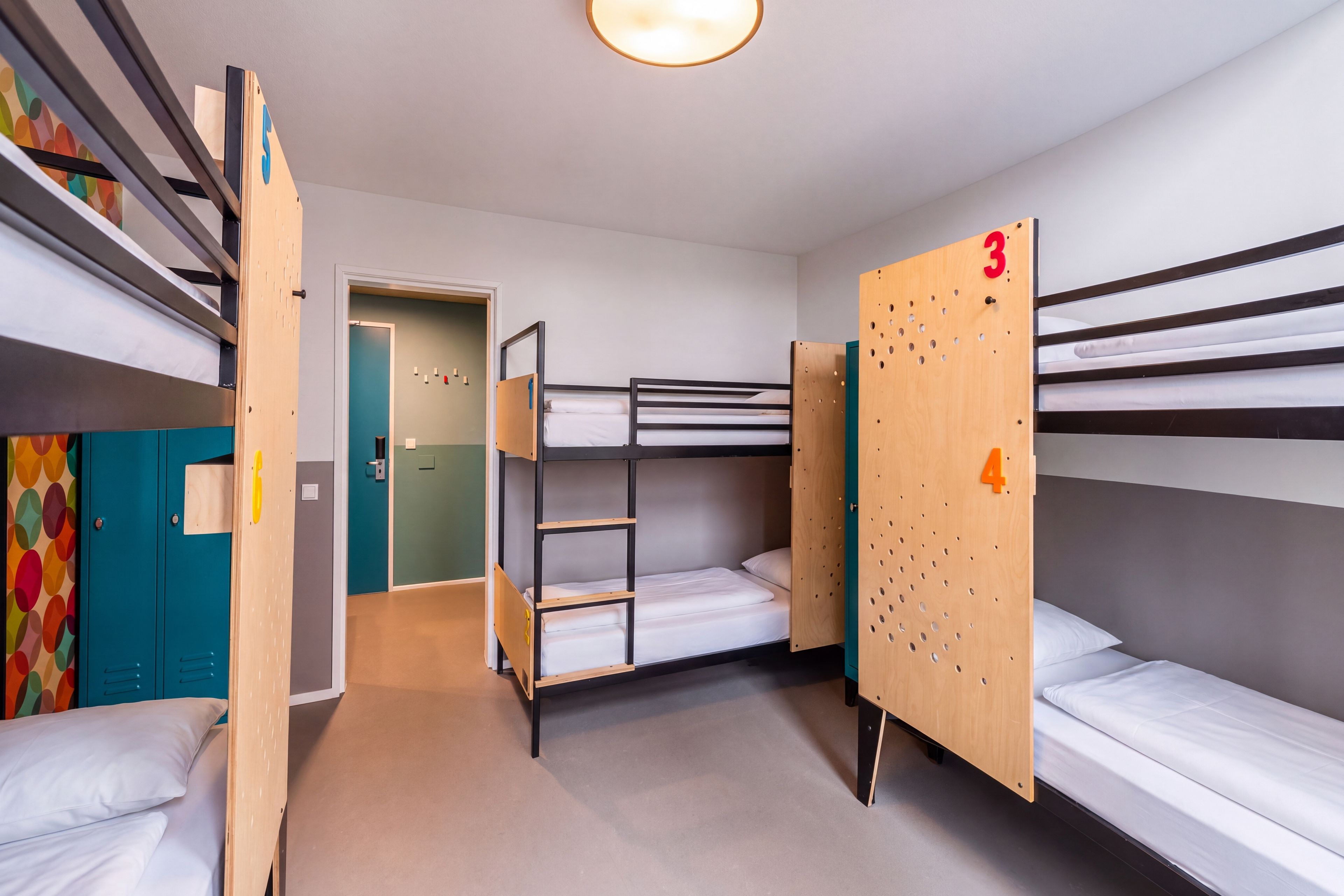 Quarto de dormitório com beliches, uma porta e uma parede com painéis numerados.