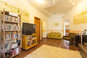 Uma sala de estar com uma estante de livros, uma televisão, um sofá amarelo e uma poltrona marrom.