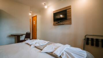 Quarto de hotel com uma cama, televisão fixada na parede, mesa com uma cadeira e uma porta.