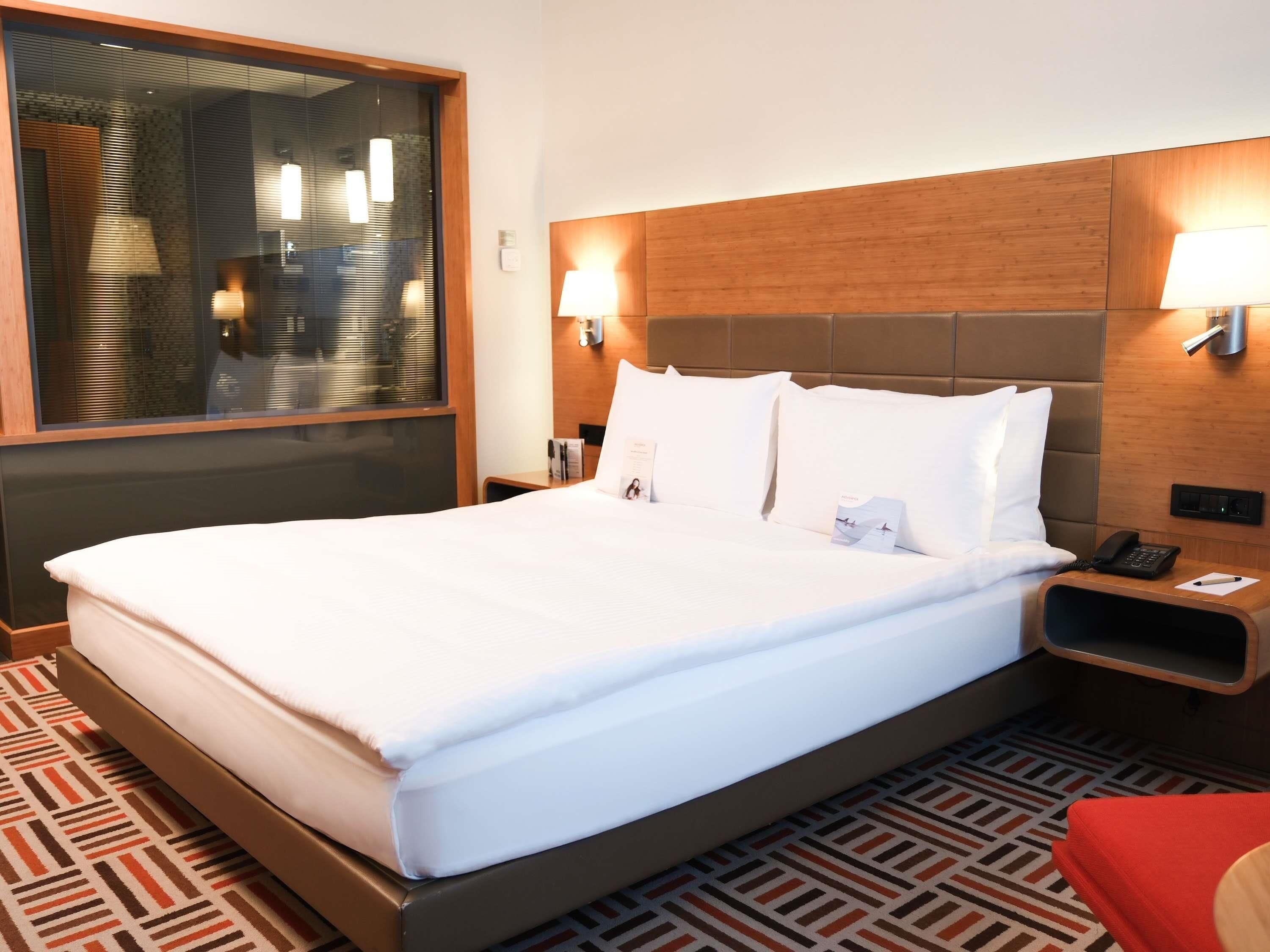 Quarto de hotel com uma cama grande, abajures, mesa de cabeceira e um espelho.