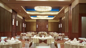 Uma sala de banquetes com mesas redondas, cadeiras brancas e um grande candelabro.