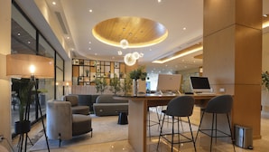 Um lobby moderno com teto curvo, balcão de recepção, banquetas de bar e área de estar com sofás e mesa de centro.