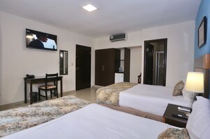 Quarto de hotel com duas camas, uma escrivaninha, televisão e uma pequena cozinha.