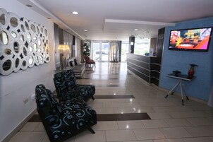 Um saguão de hotel com balcão de recepção, área de estar e uma televisão na parede.
