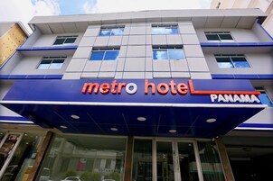 Um hotel chamado Metro Hotel Panama com fachada moderna, grandes janelas e uma placa azul e laranja bem visível.