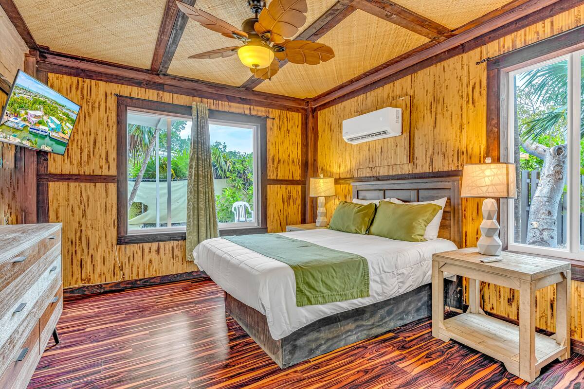 Quarto com decoração em madeira, com cama, mesas de cabeceira e ventoinha no teto.